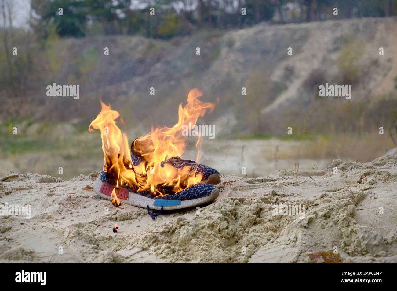 Burning sports sneakers or gym shoes on fire stand on sandy beach coast ...