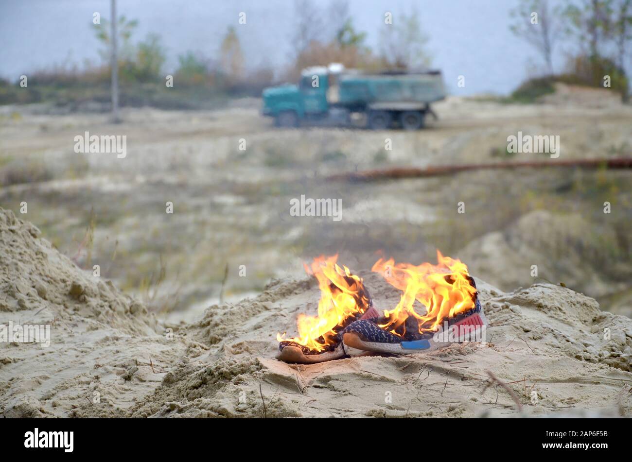 Burning sports sneakers or gym shoes on fire stand on sandy beach coast ...