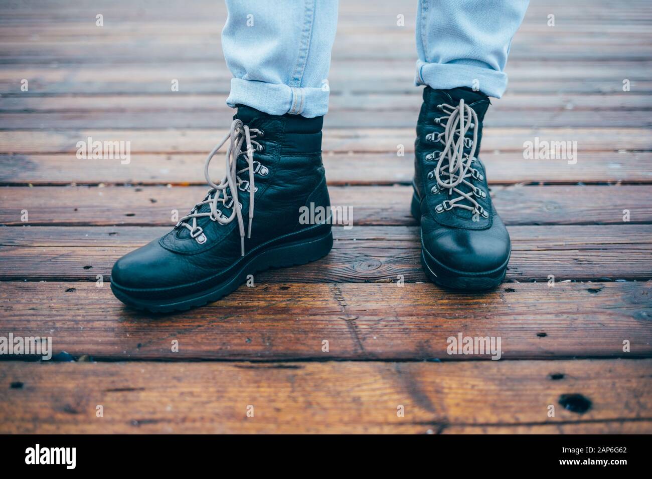 Close-up of female legs in jeans shod in rough boots standing on wet ...