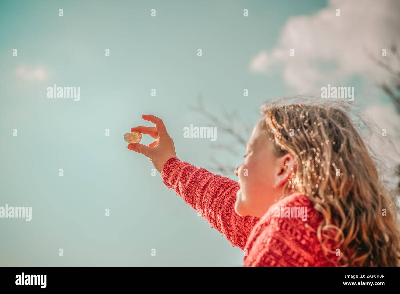 Beautiful blonde girl holding Heart shaped stone in hands, blue sky in ...