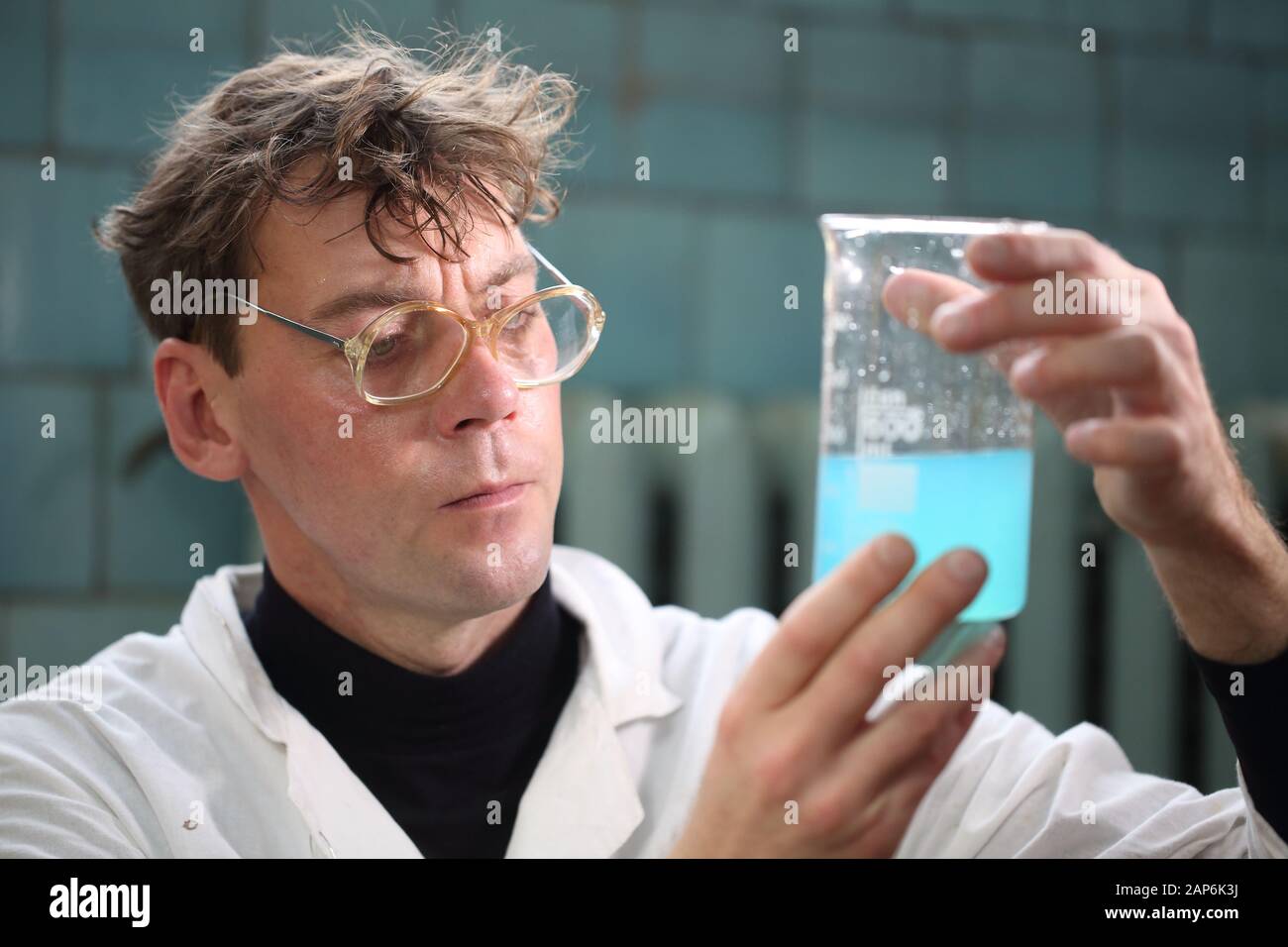 A scientist in a white coat is holding a beaker with a blue reagent ...