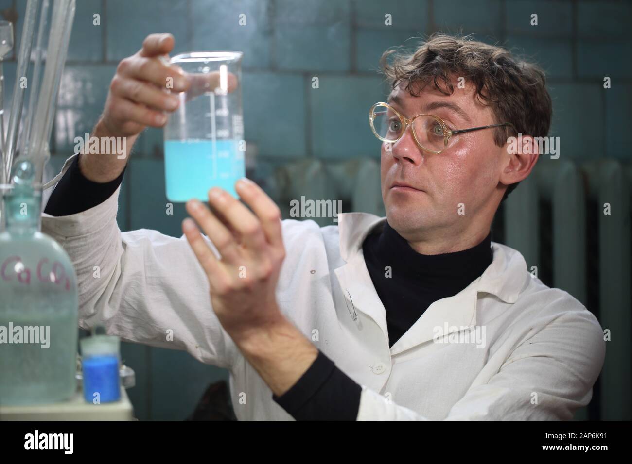 A scientist in a white coat is holding a beaker with a blue reagent ...