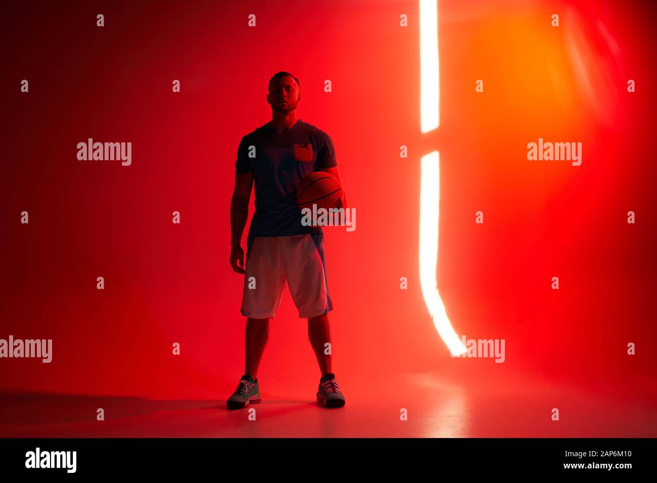 Young athletic man, basketball player stands holding ball in one hand ...