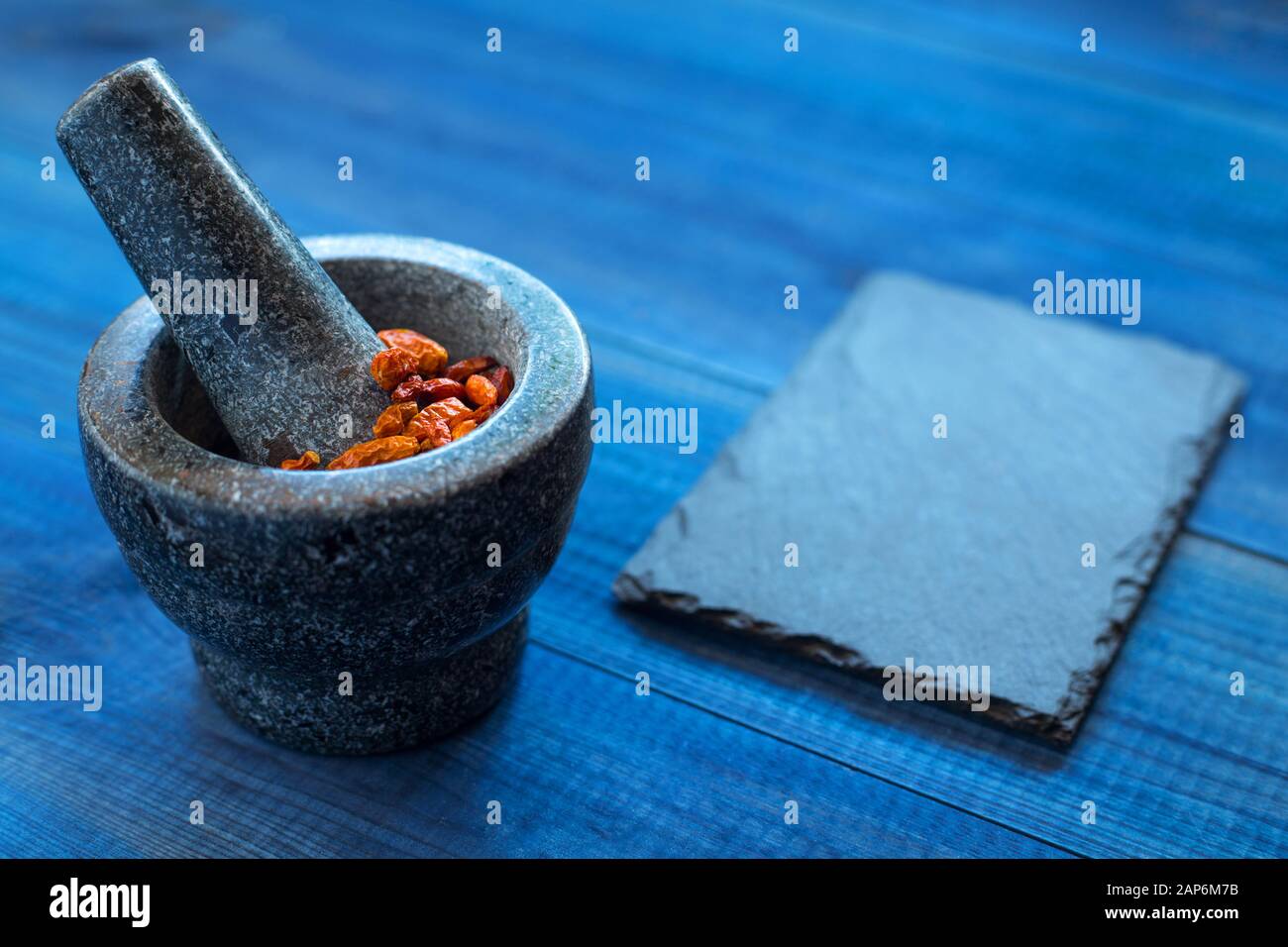 chilli peperoncini peppers in stone granite mortar on blue wooden desk ...