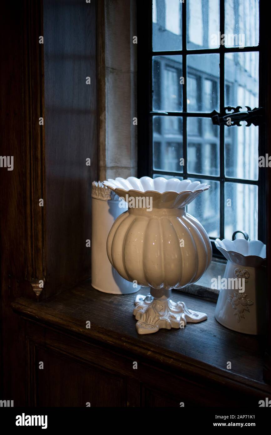 A large white porcelain vase stands on a wooden window sill of an old ...
