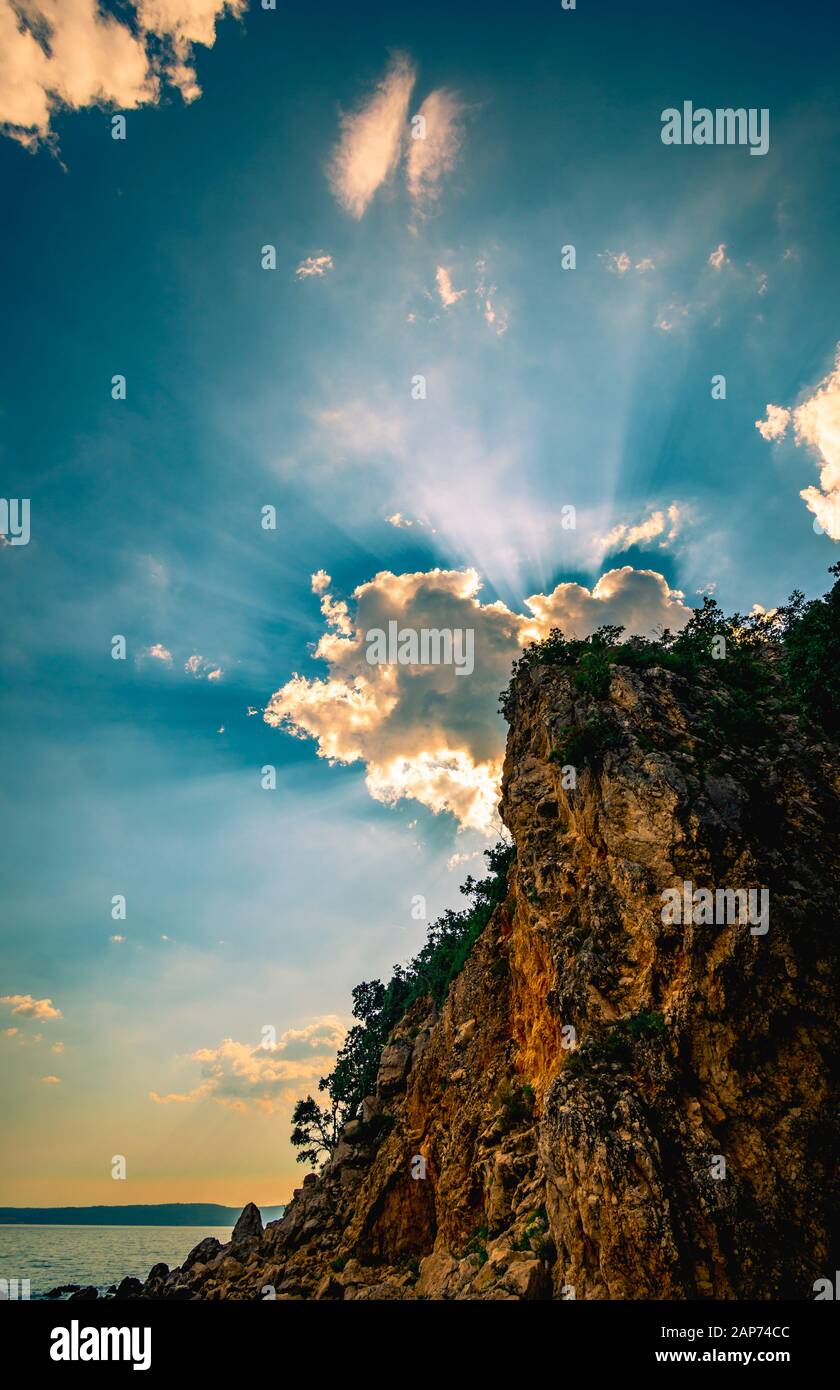 Sun rays shine past the clouds behind an impressive rock Stock Photo ...