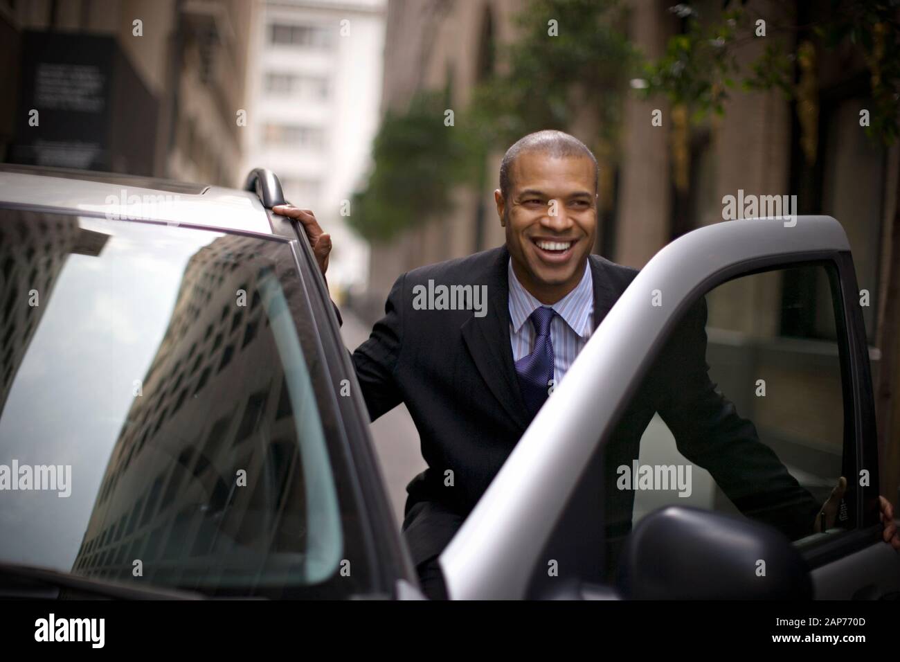 Smiling mid-adult business man getting inside a car on a city street ...