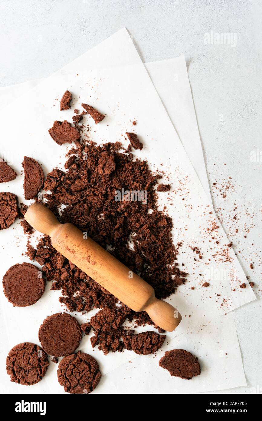 A wooden rolling pin crushing chocolate cookies in preparation for a ...