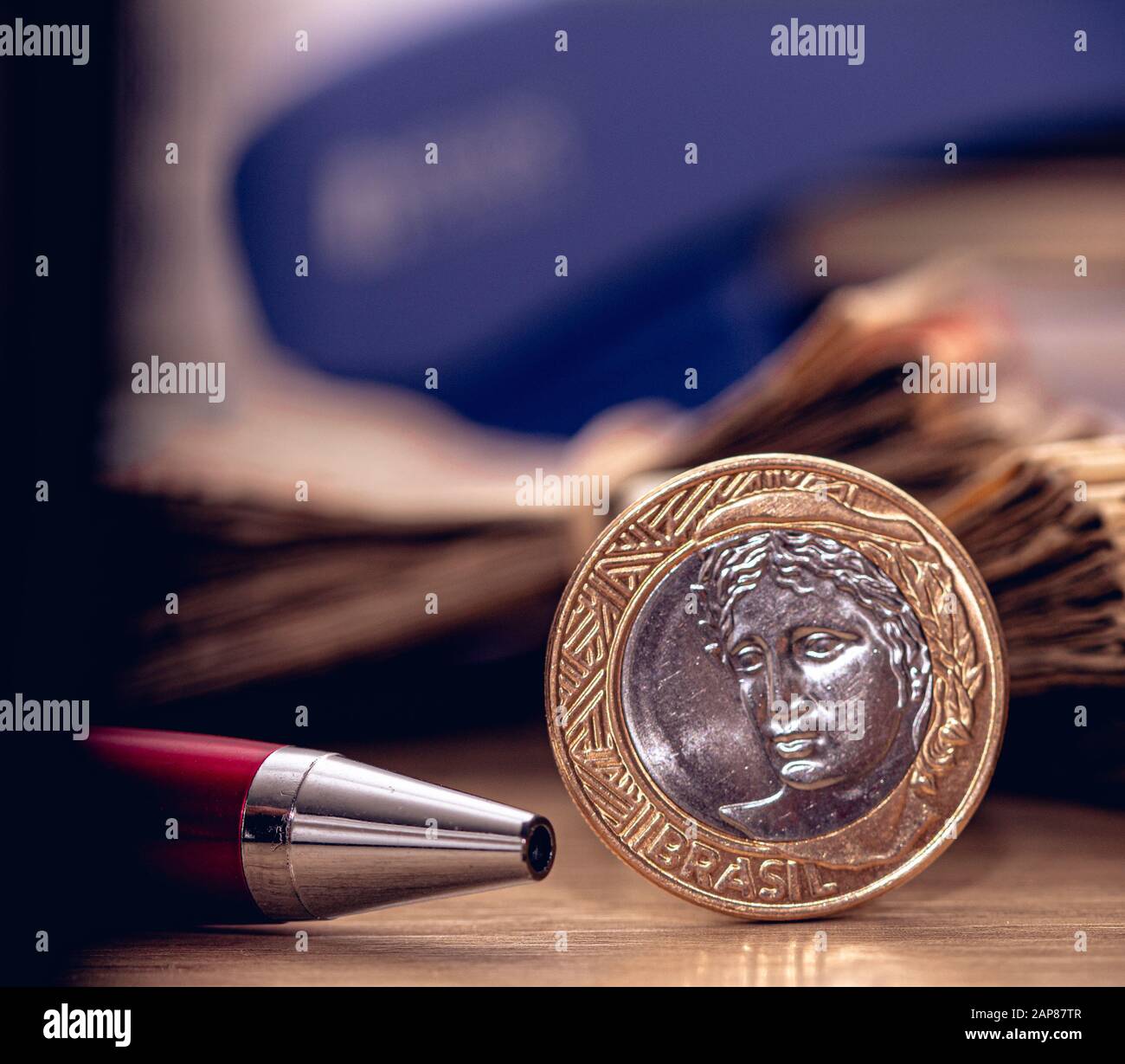 Brazilian currency. A one Real coin standing on the table between a pen ...