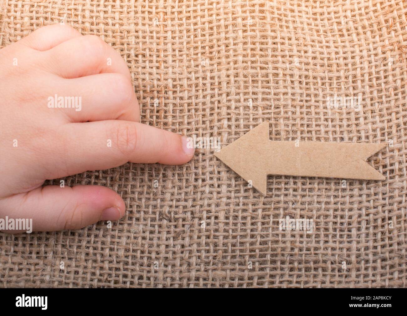 Arrow sign cut out of brown paper against a f'iger on canvas Stock ...