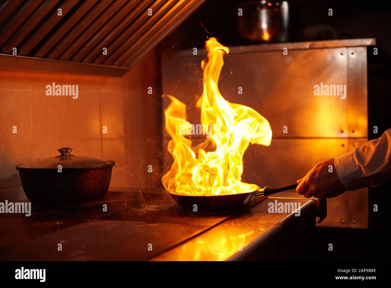 Flambe. Fire in frying pan. Professional chef in a commercial kitchen ...