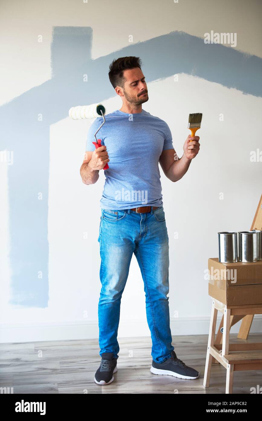 Young man choosing between paint roller and paintbrush Stock Photo - Alamy