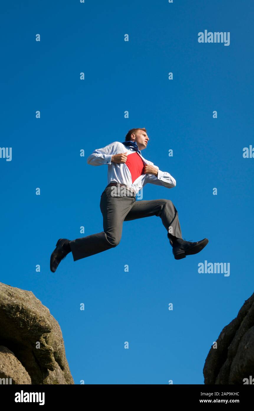 Superhero businessman taking a daring leap between two boulders ...