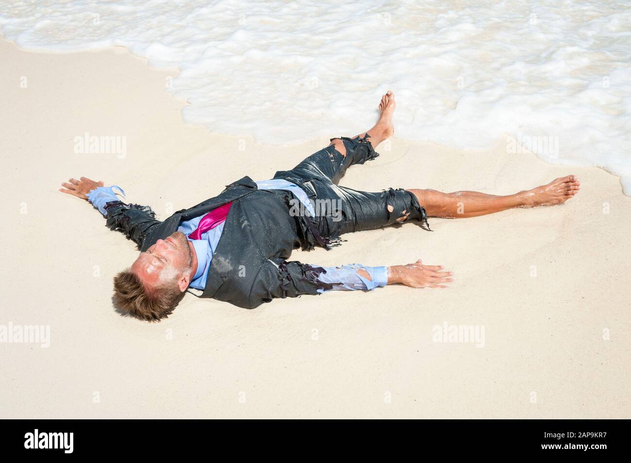 Castaway survivor businessman washed up on a tropical beach in a ragged ...