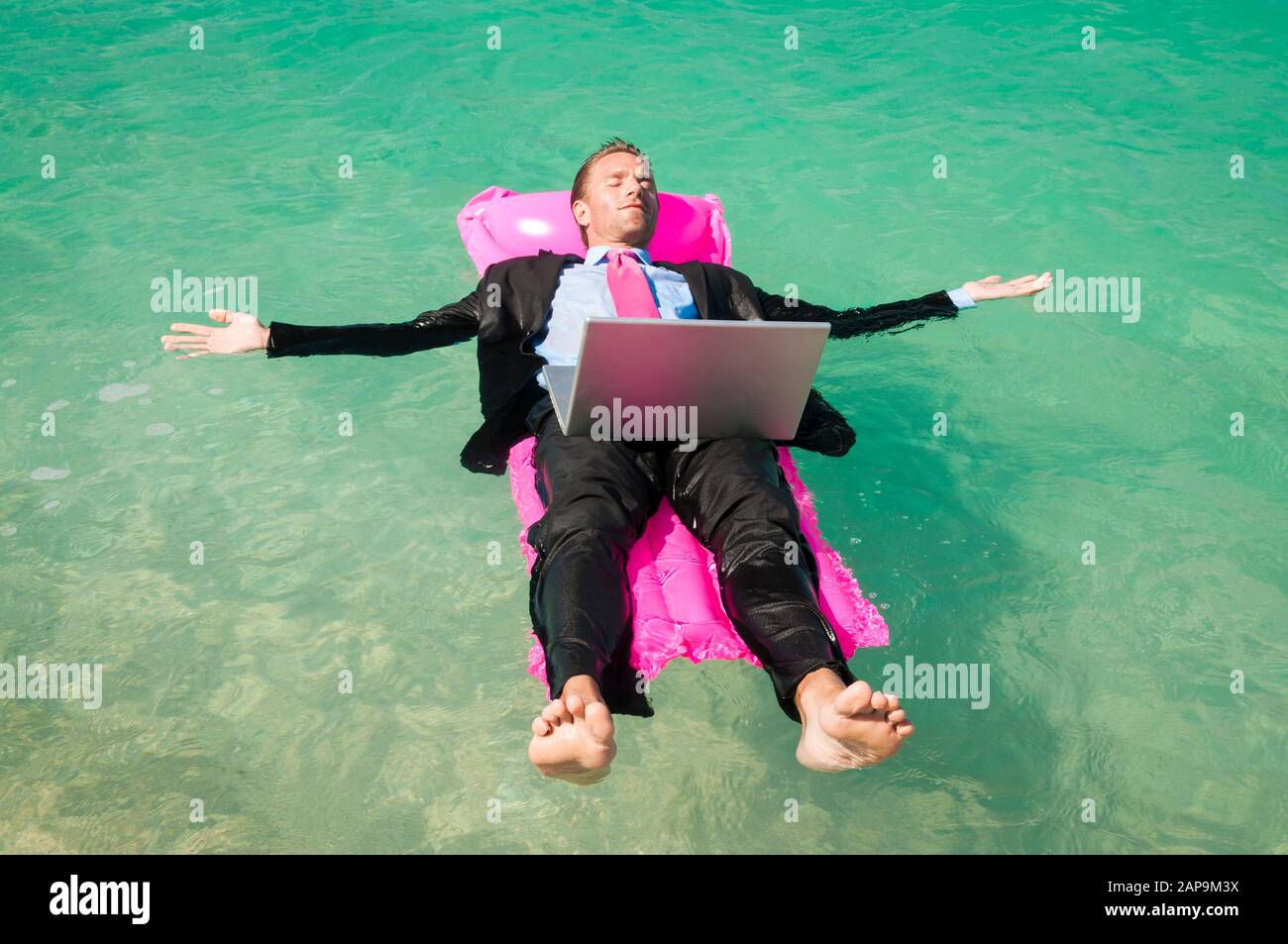 Barefoot businessman floating outdoors with laptop computer on a pink ...