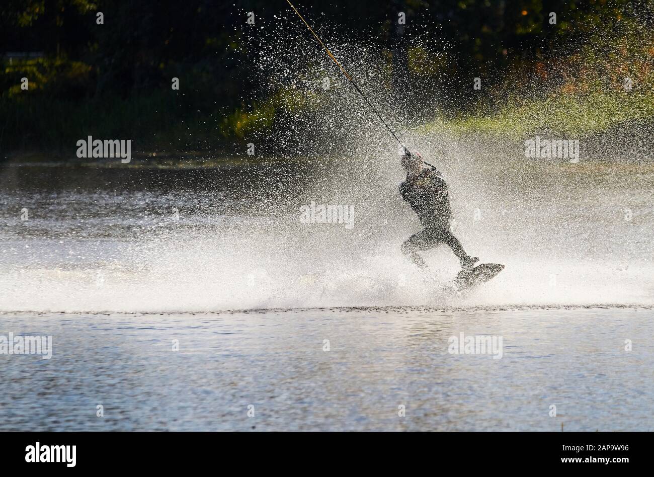 Wakeboarder surfing across a lake with water splashing. This is an ...