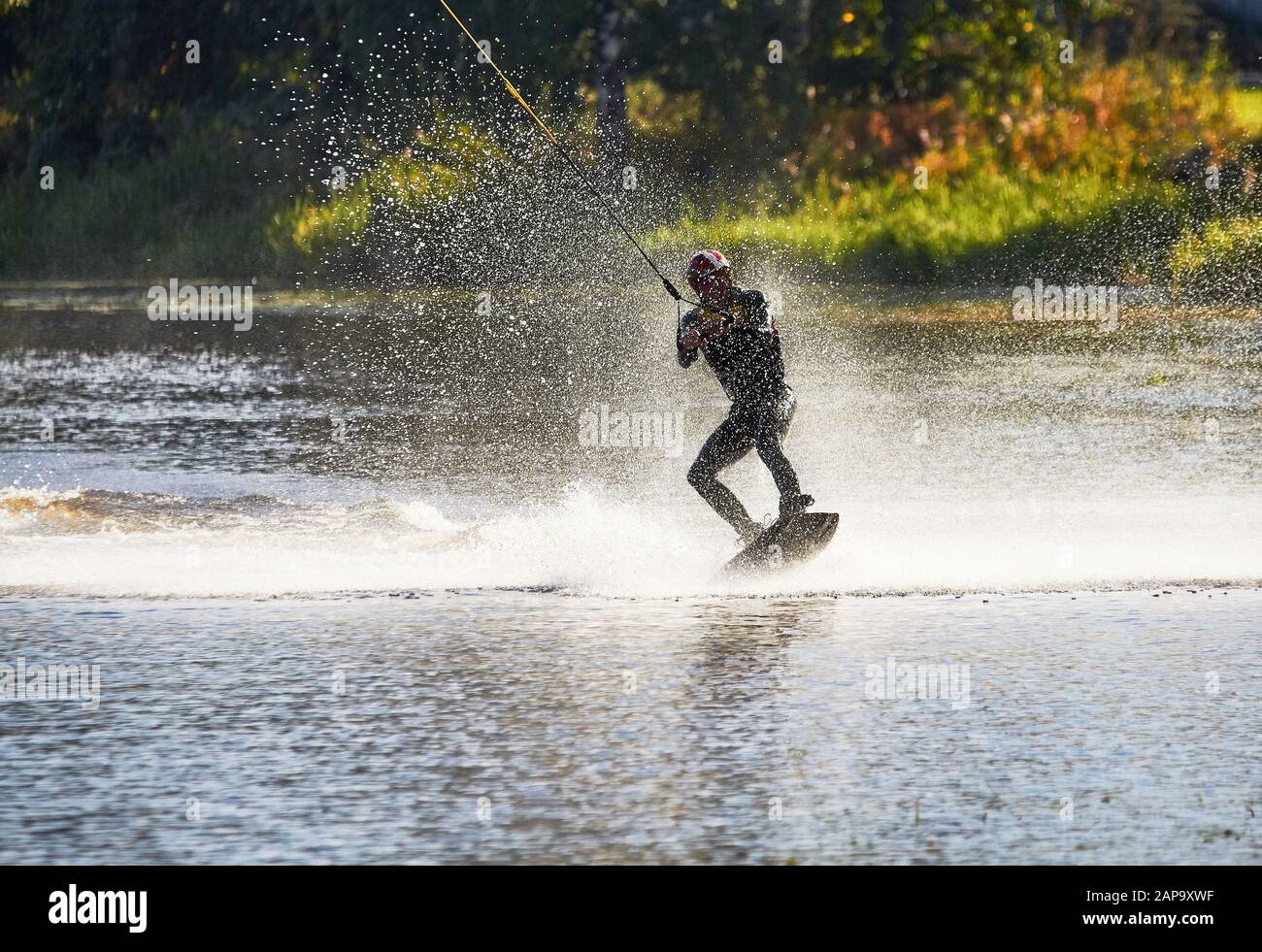 Wakeboarder surfing across a lake with water splashing. This is an ...