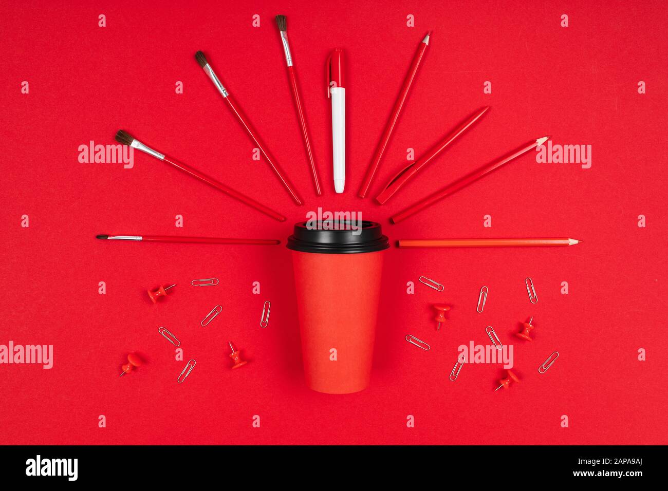 Brushes, paper clips, marker around a cup of coffee isolated on red ...