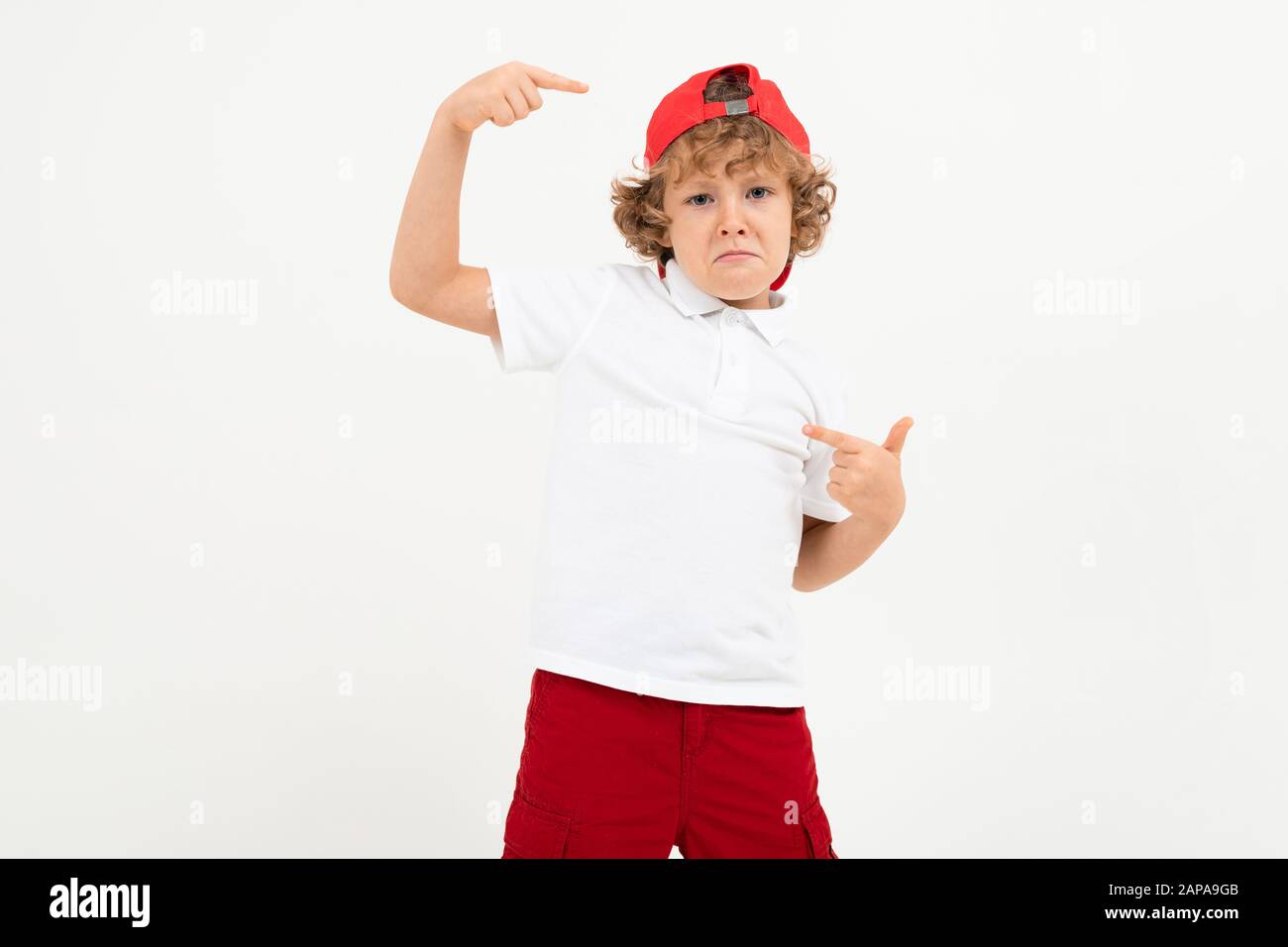 Caucasian boy in white t-shirt, red cap, red shorts smiles isolated on ...