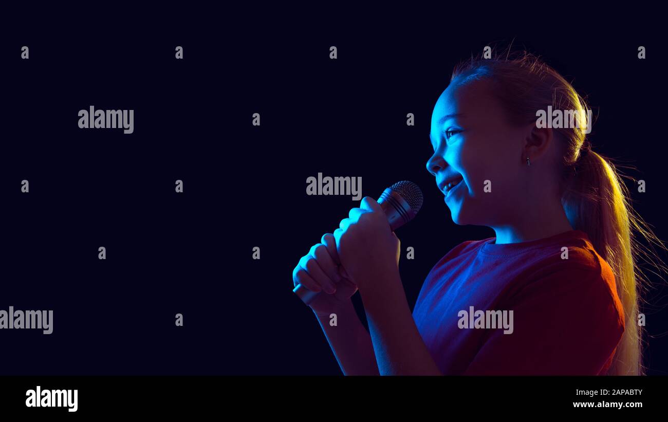 Singing happy. Caucasian girl's portrait on dark background in neon ...