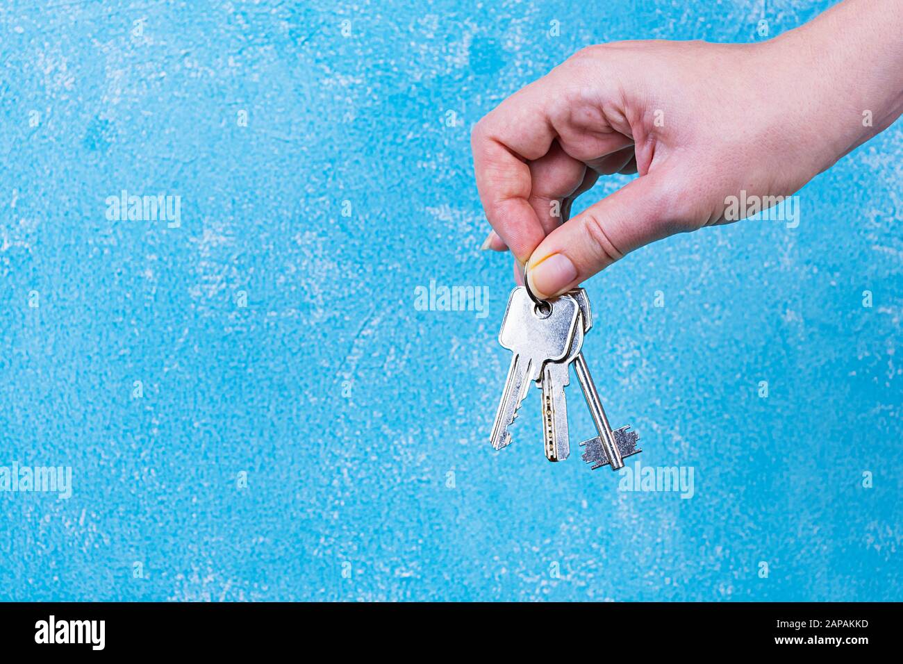 Female hand holding keys on blue background Stock Photo - Alamy