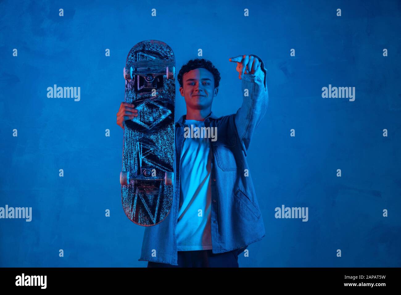 Caucasian young skateboarder in casual pointing on dark neon lighted ...