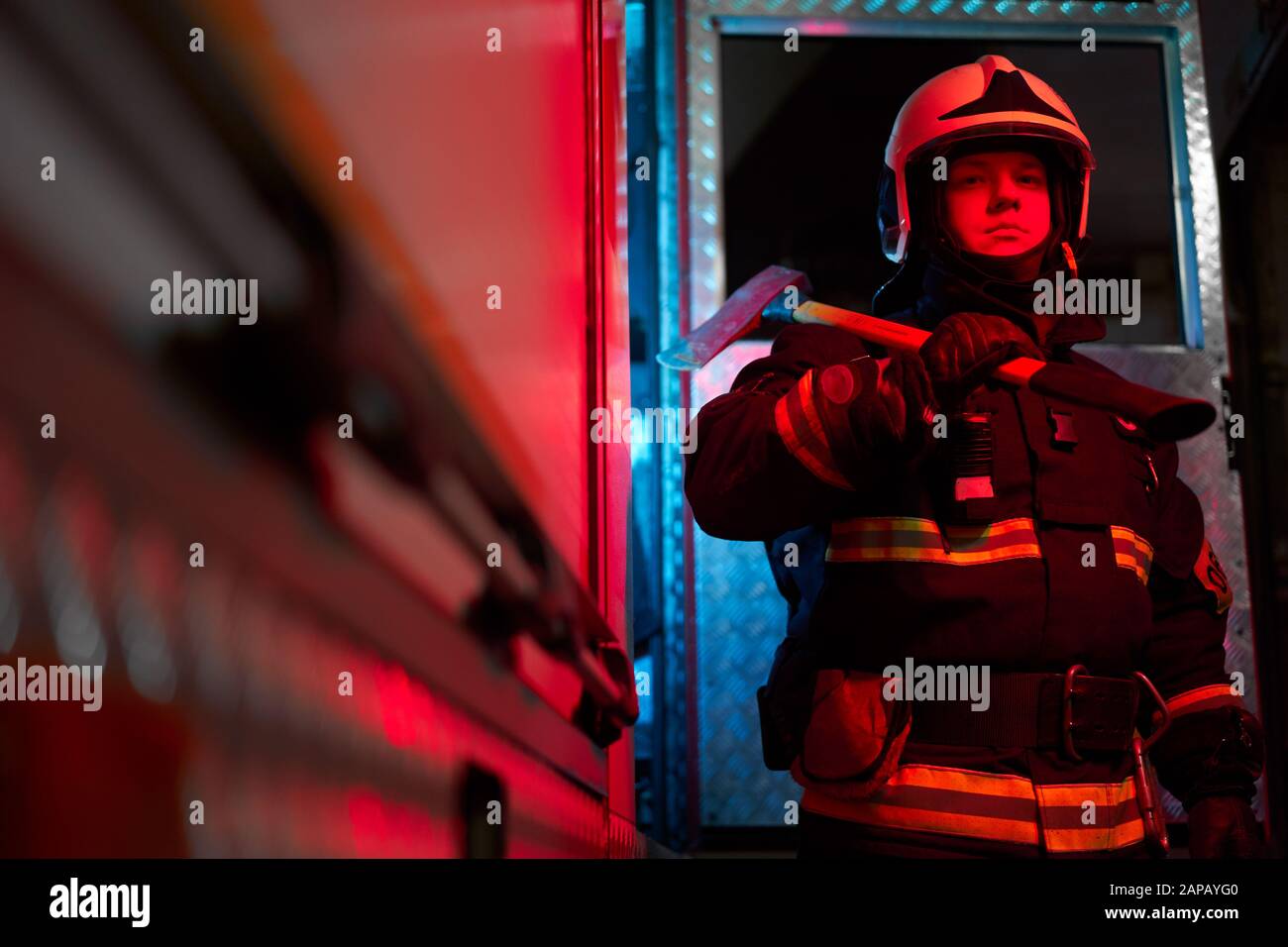Firefighter male with hammer on his shoulder standing near fire engine ...