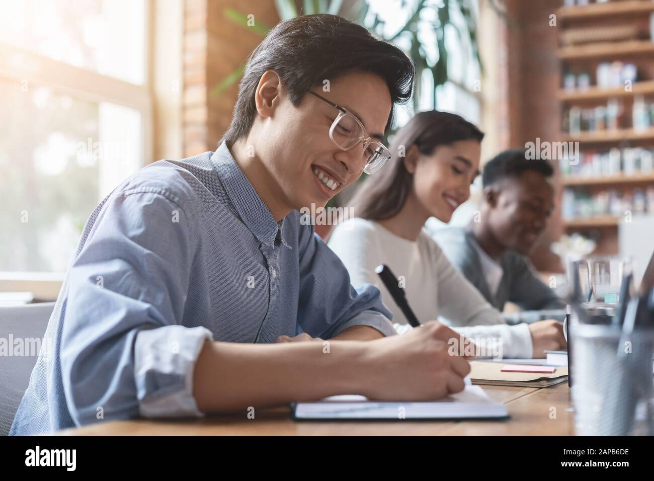 Young asian guy taking notes, having business meeting with colleagues ...