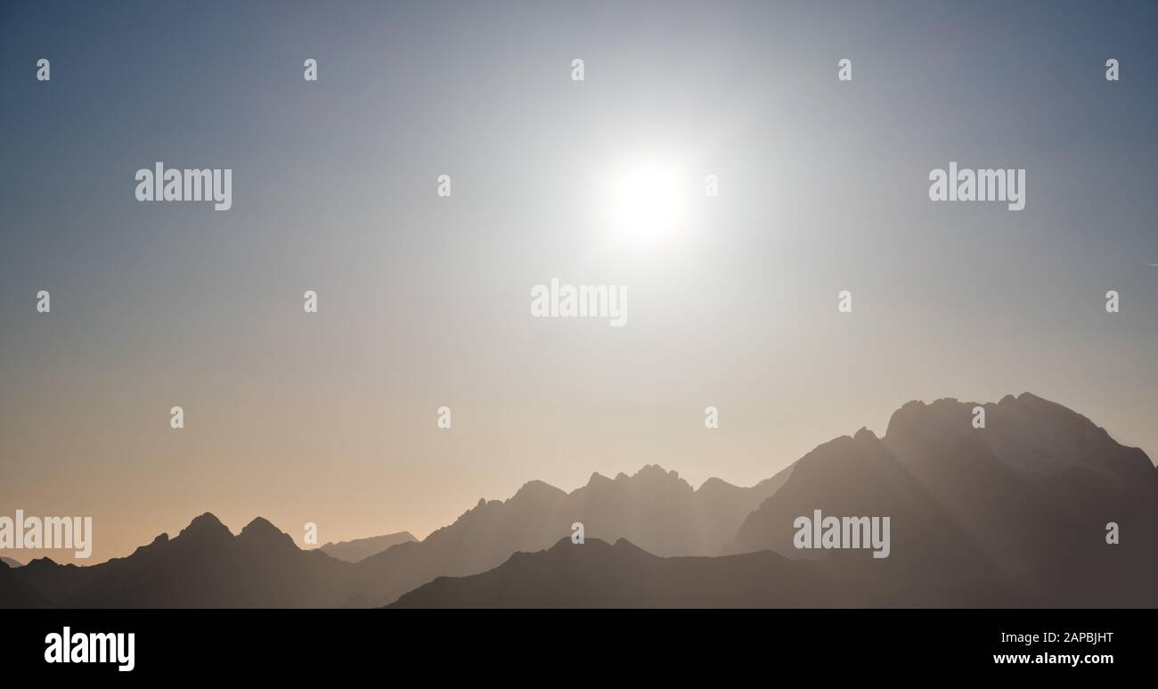 Sun glow in evening misty sky view. Mountain tops silhouettes in clouds ...