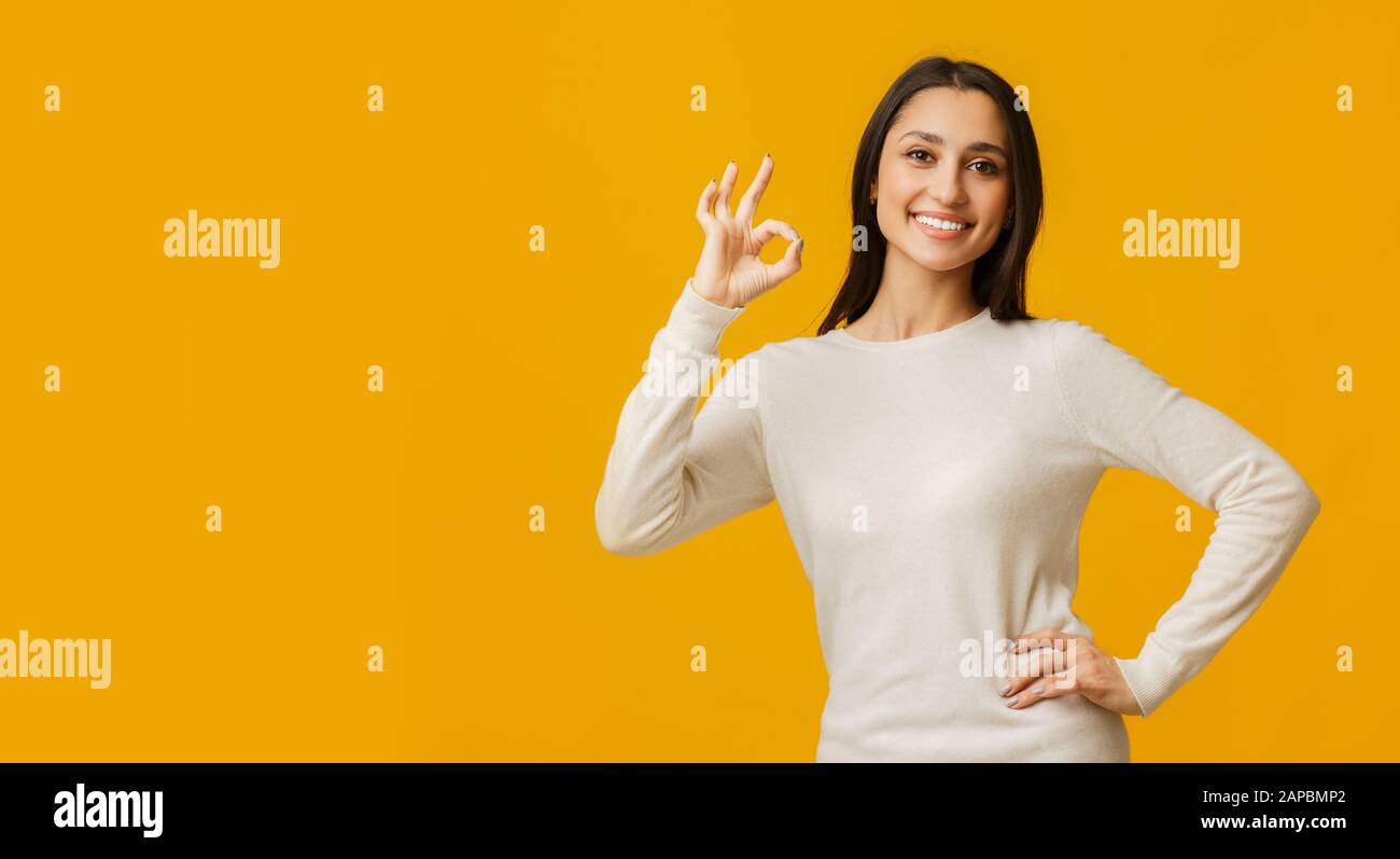 Optimistic millennial girl showing ok gesture while posing over yellow ...