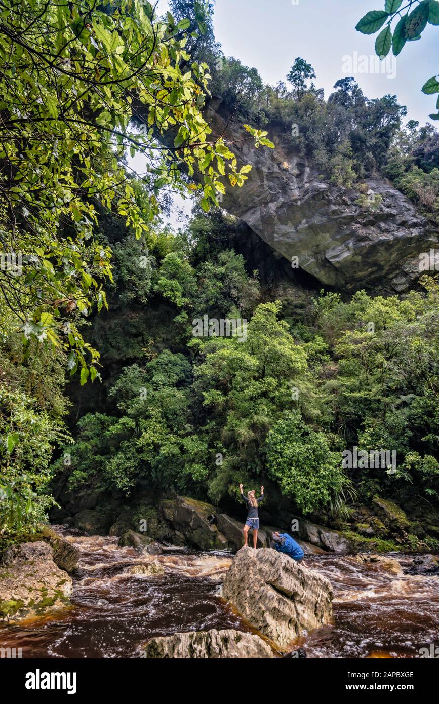 Hikers looking at Oparara Arch, on boulder at Oparara River, rain ...