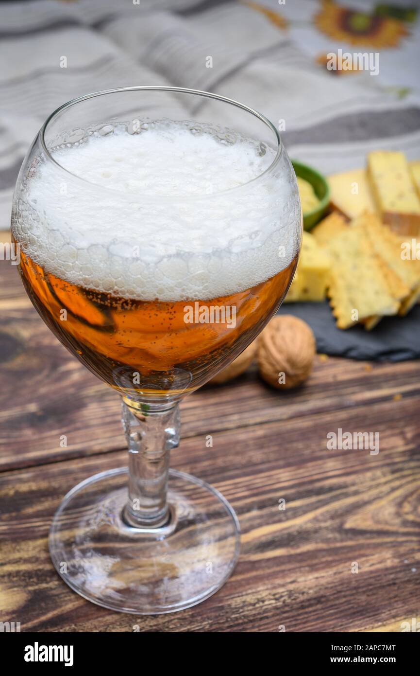 Glass of Belgian abbey blond beer and stone plate with cheeses made by ...
