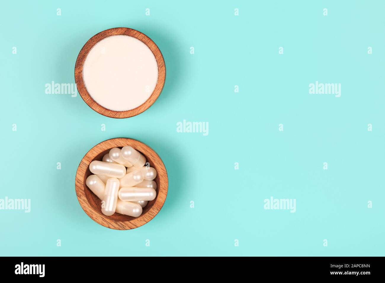 Collagen in capsules and in powder in two wooden bowls on pastel blue ...