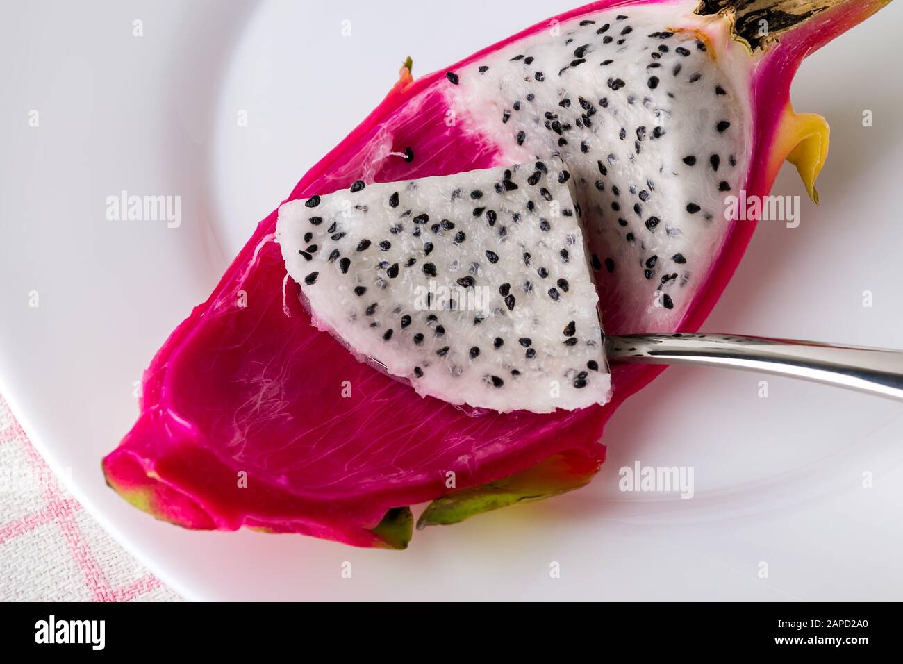 Taking a dragon fruit or pitaya pulp with a spoon on a white plate ...