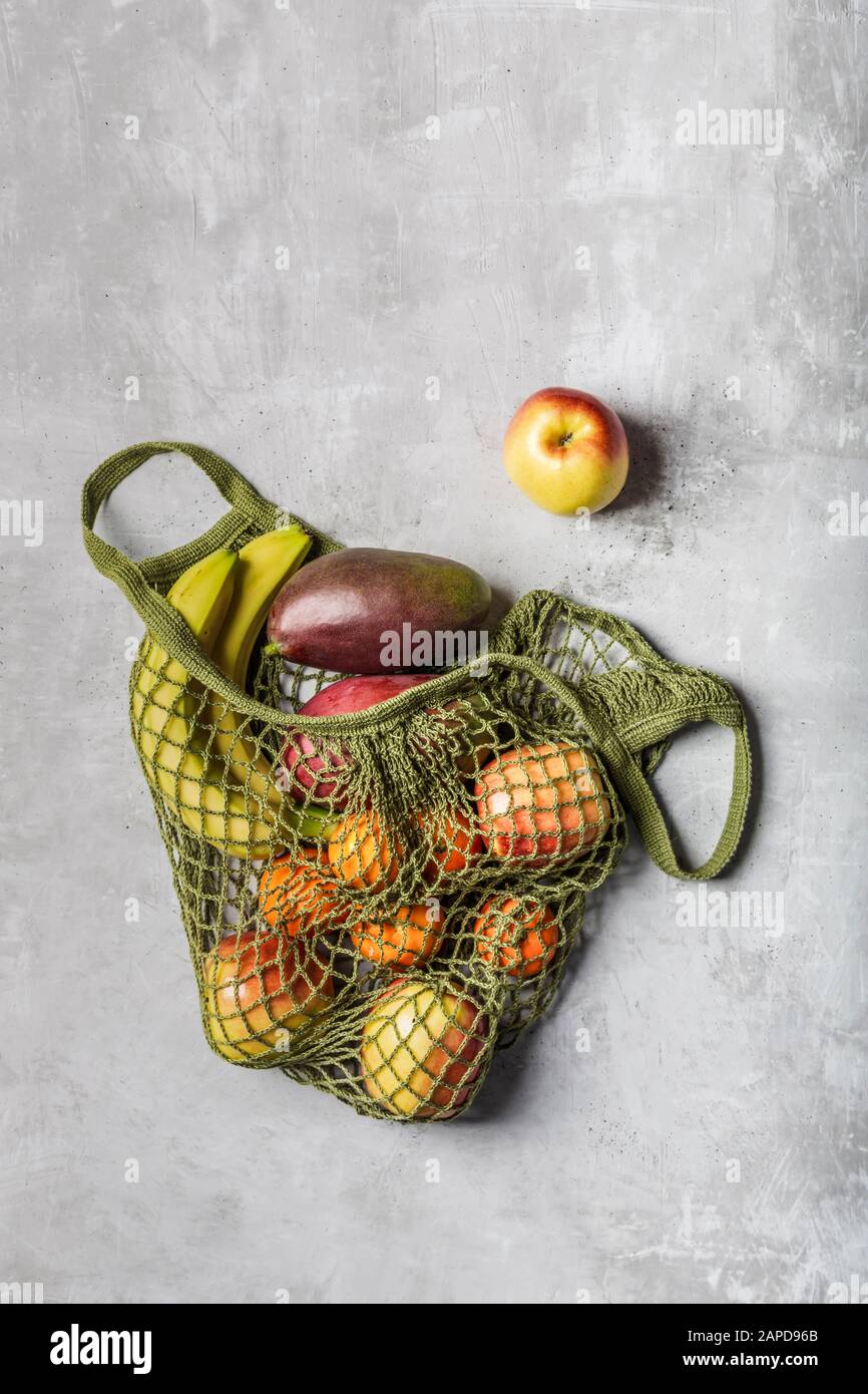 Fresh fruit in a green string bag on a light gray background. Bananas ...