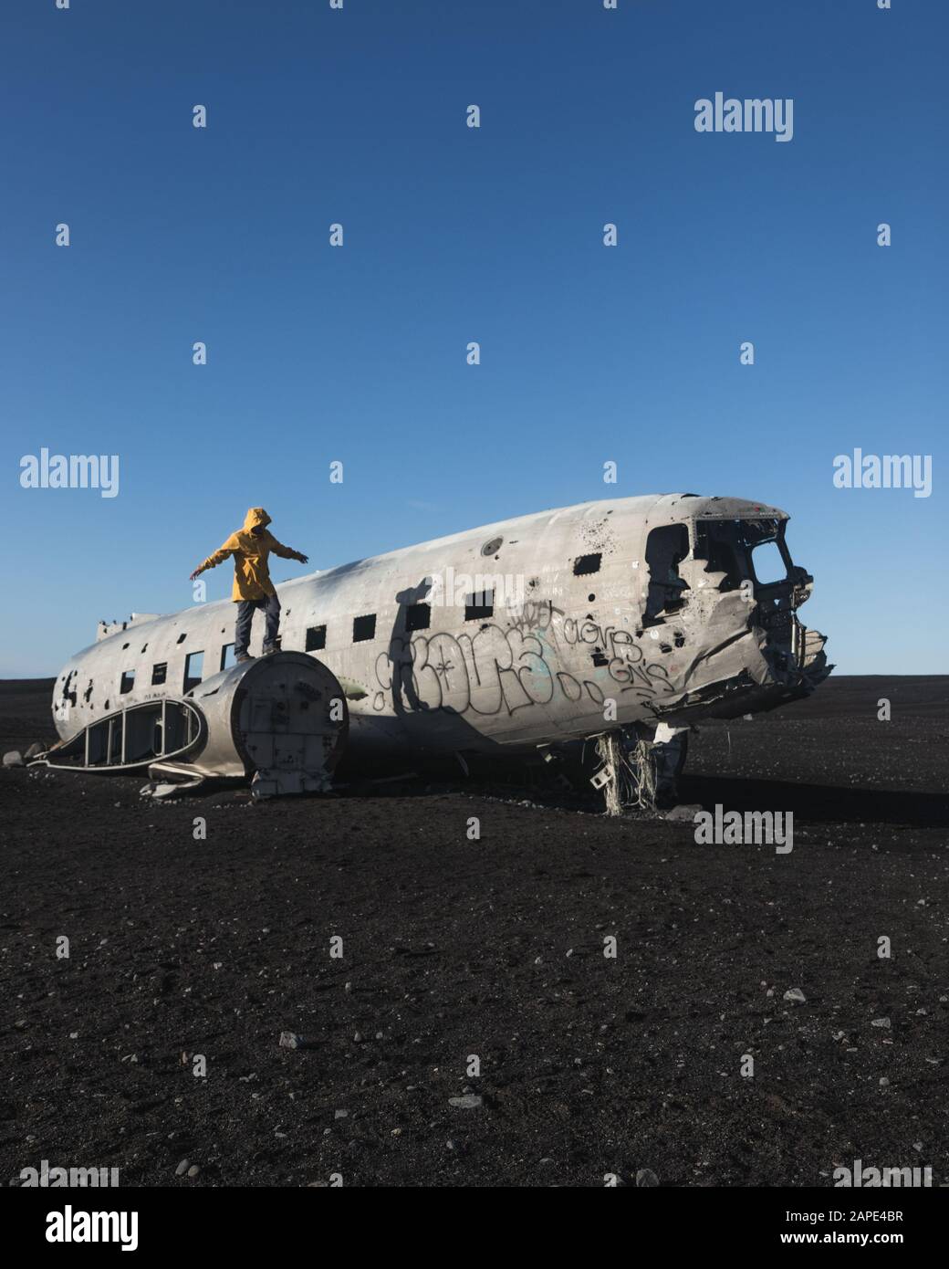 Man standing on an abandoned crashed plane with a clear blue sky ...