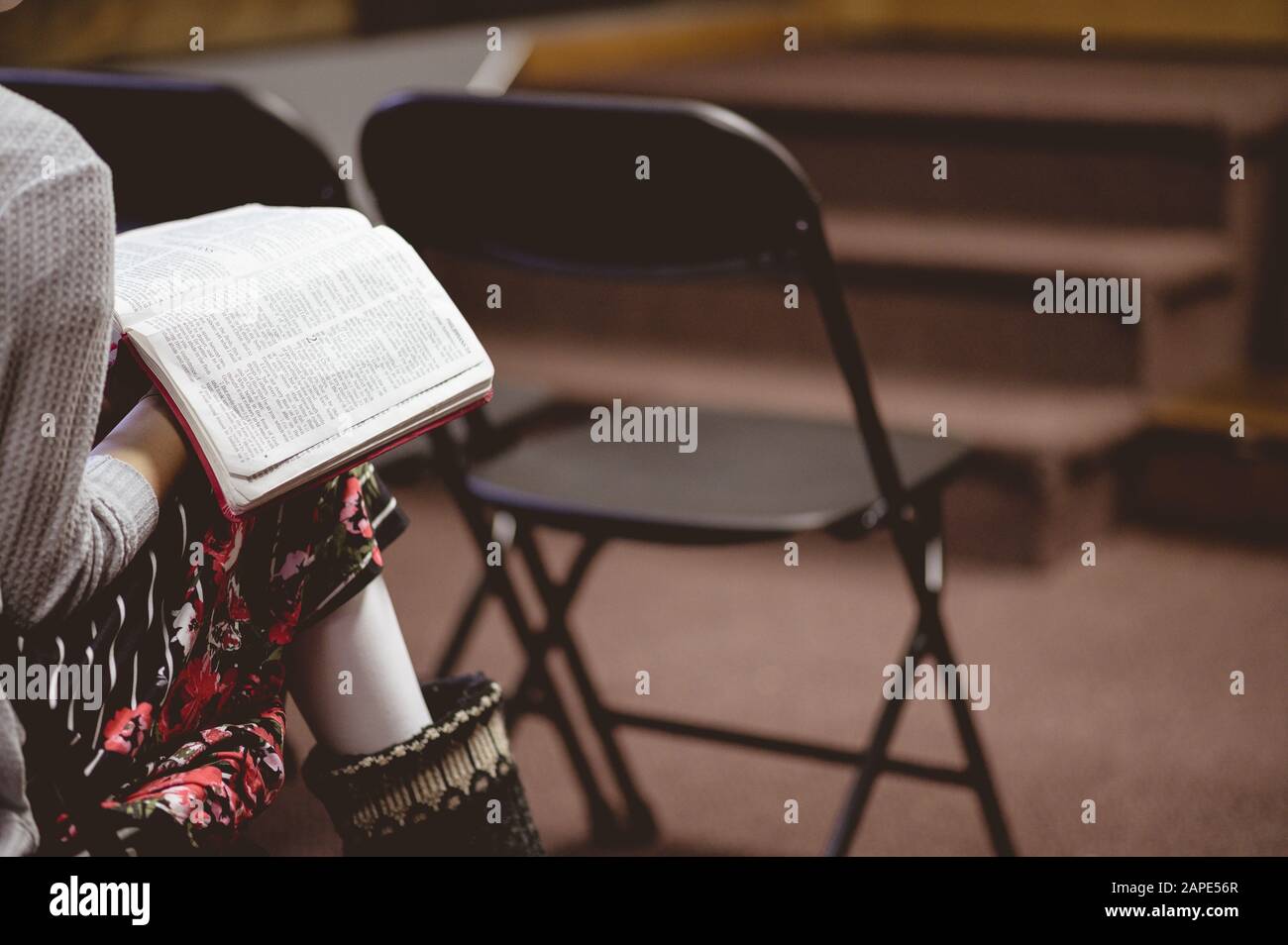 Closeup of a person sitting on a chair and reading a bible in a church ...