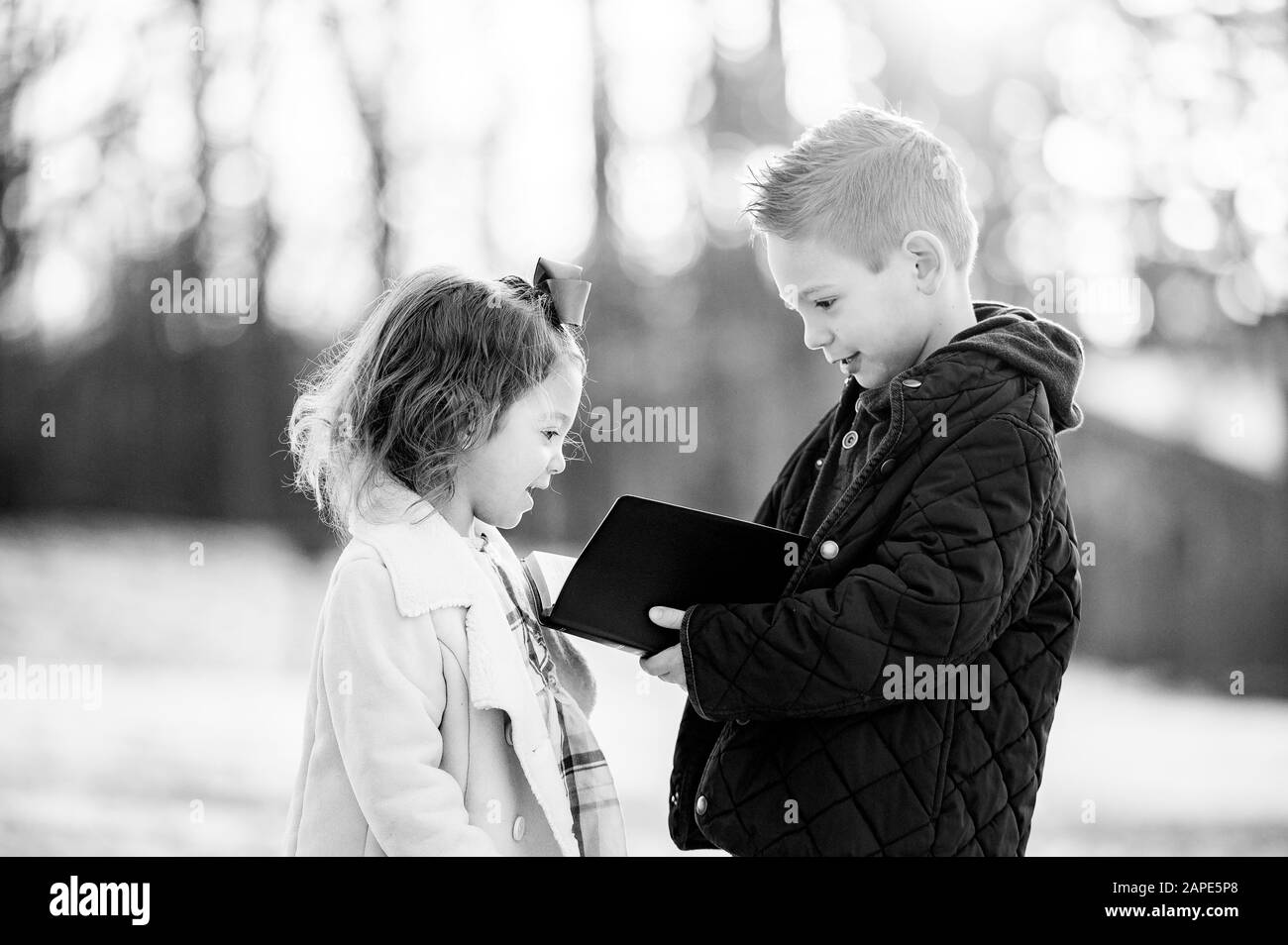 Greyscale of two kids reading the bible in a garden covered in the snow ...