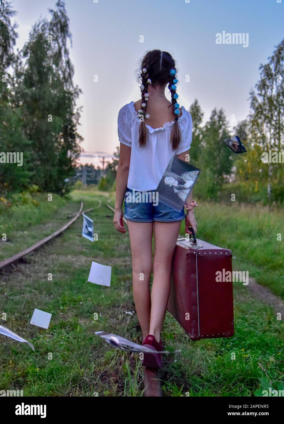 A teenage girl walks along the railway tracks with a heavy old suitcase ...