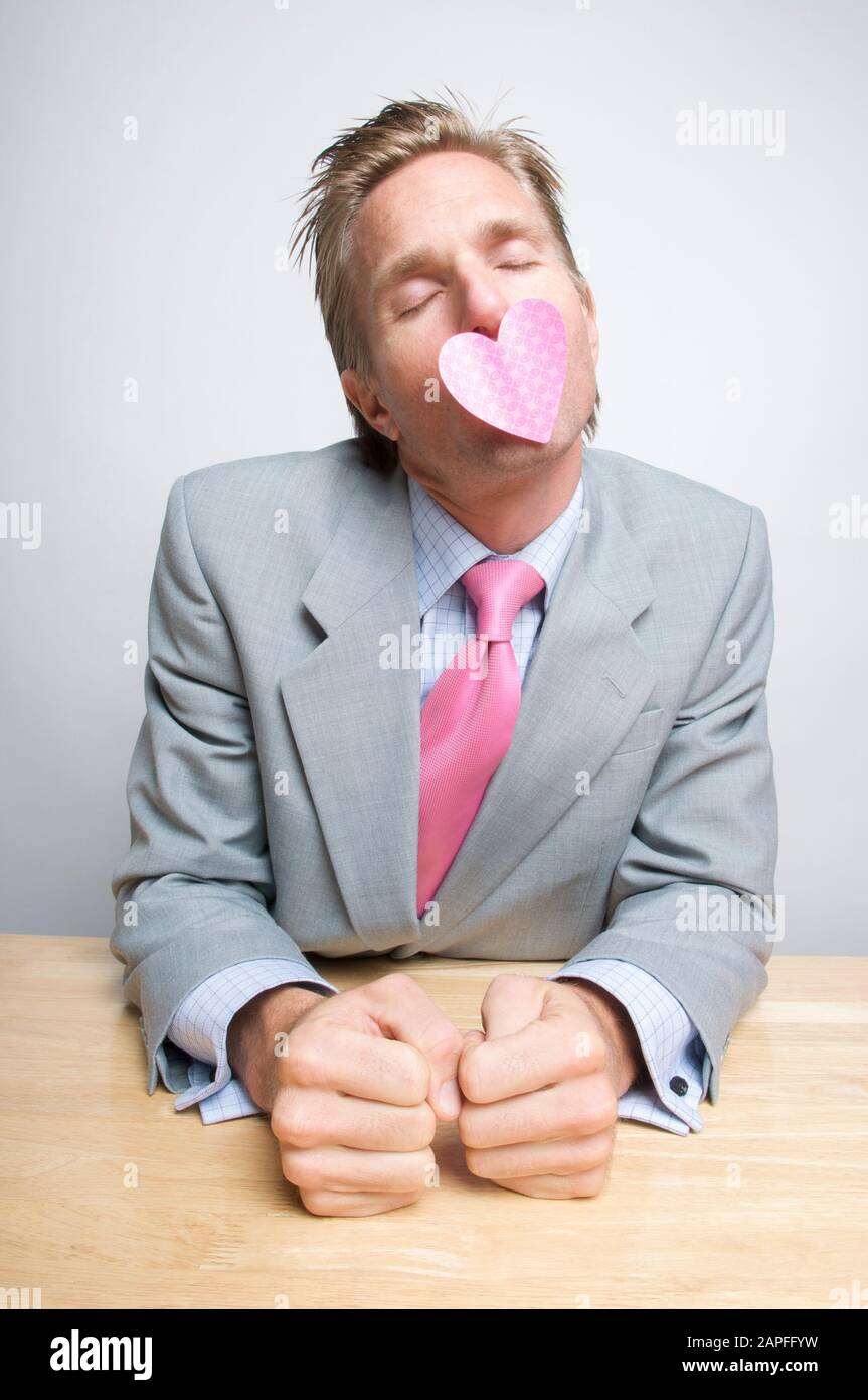 Flirty office worker sitting at his desk with a heart stuck to his lips ...