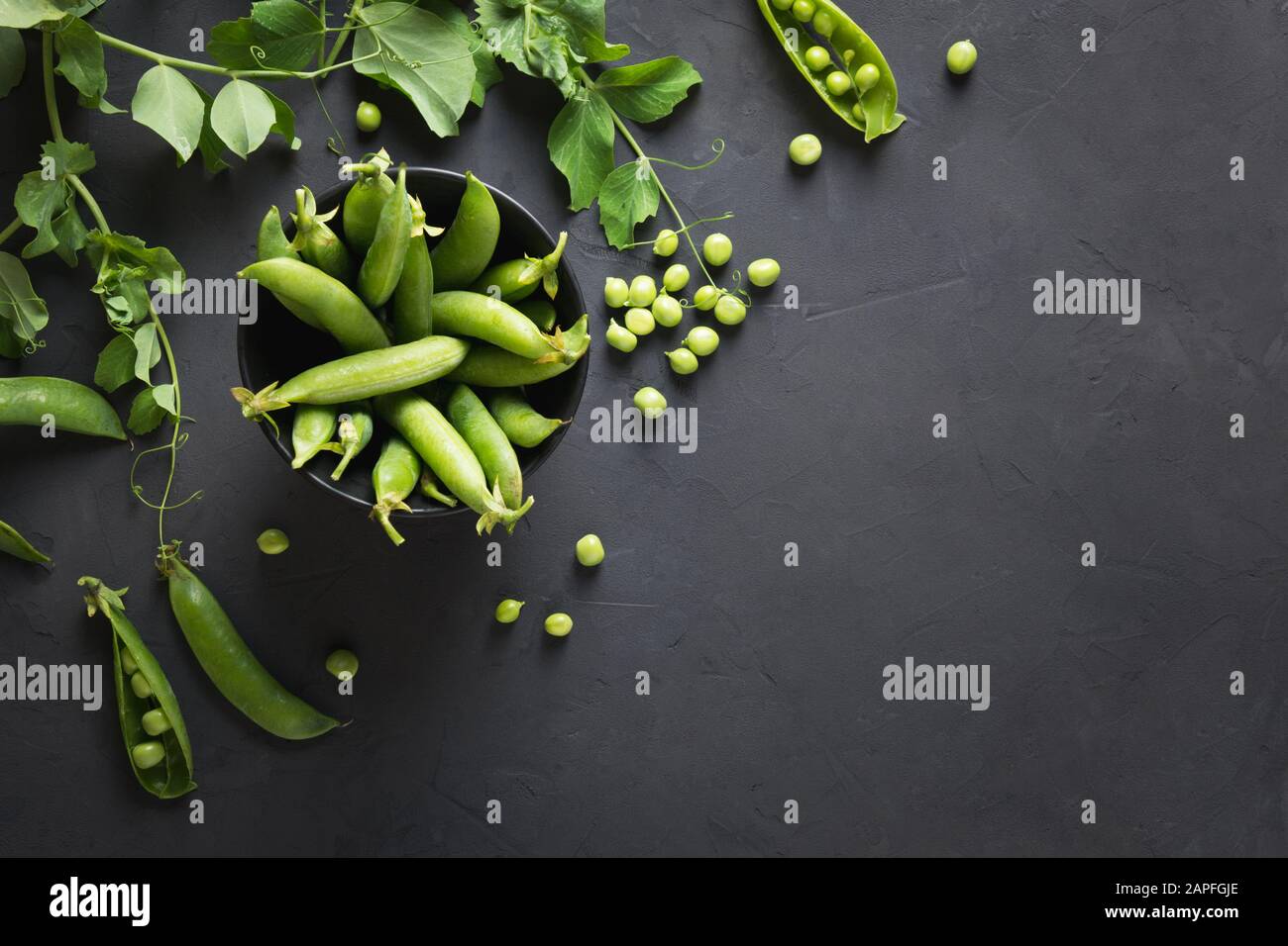 Green fresh pea seeds and branches on black background. Space for text ...