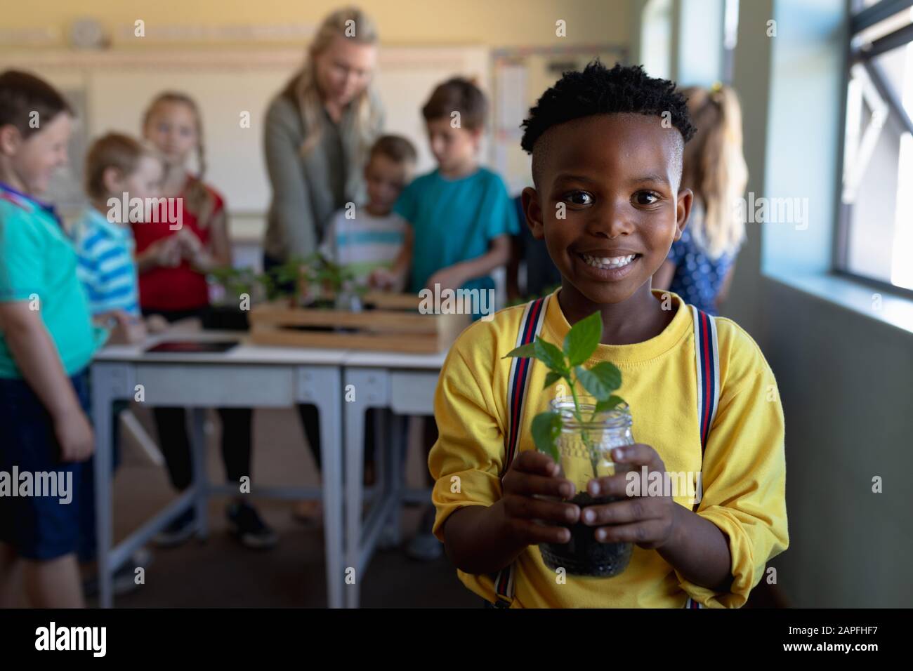 Schoolboy standing holding a seedling plant in a jar of earth in an ...