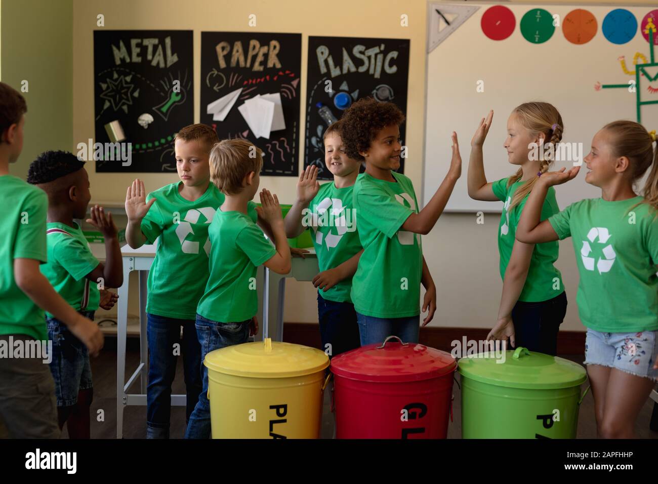 Group of schoolchildren holding color coded recycling bins and bags in ...