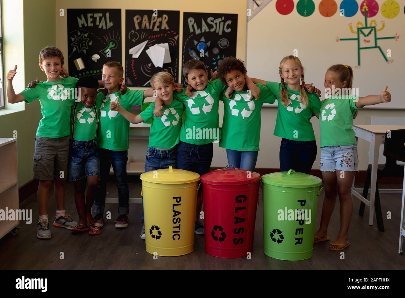 Group of schoolchildren holding color coded recycling bins and bags in ...