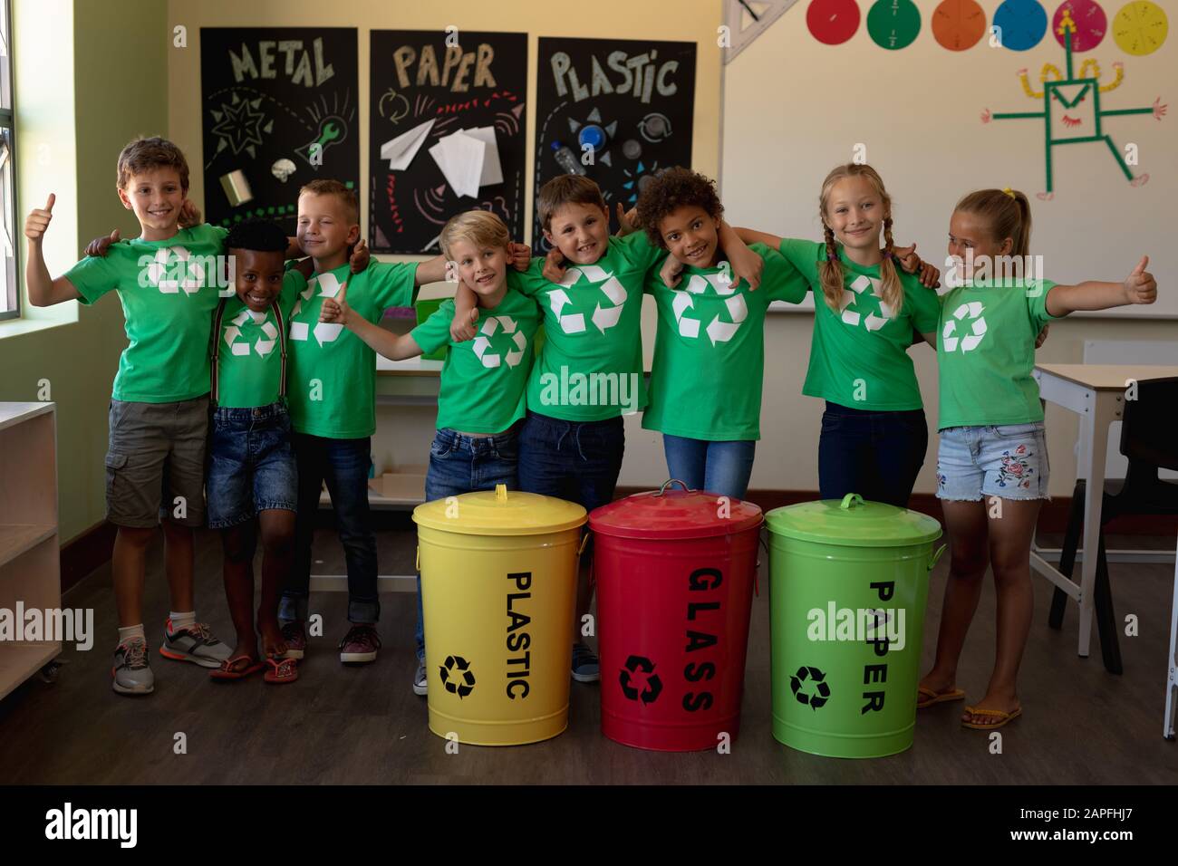 Group of schoolchildren holding color coded recycling bins and bags in ...