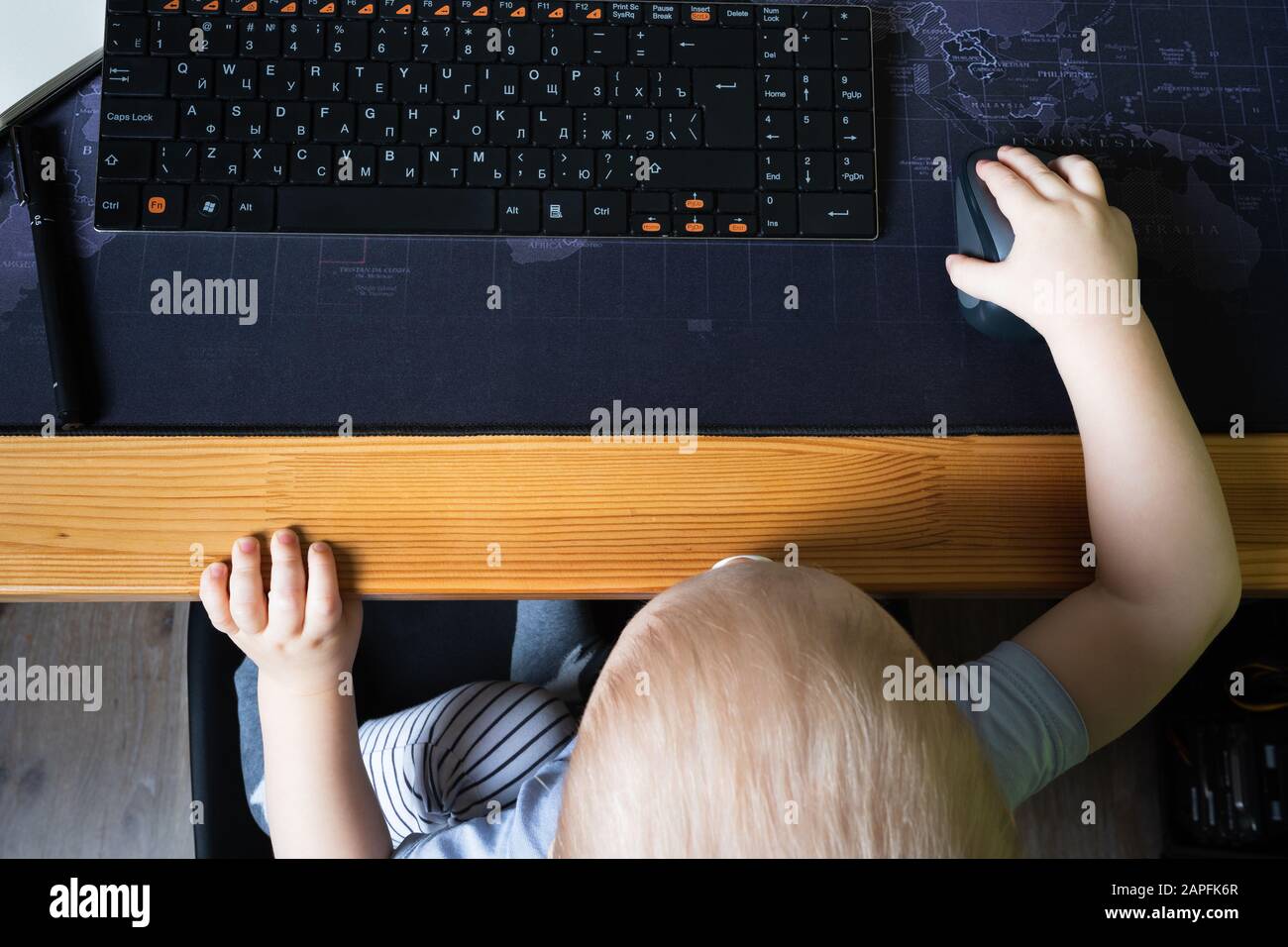 Top view of little boy sits at a computer and holds a keyboard in his ...