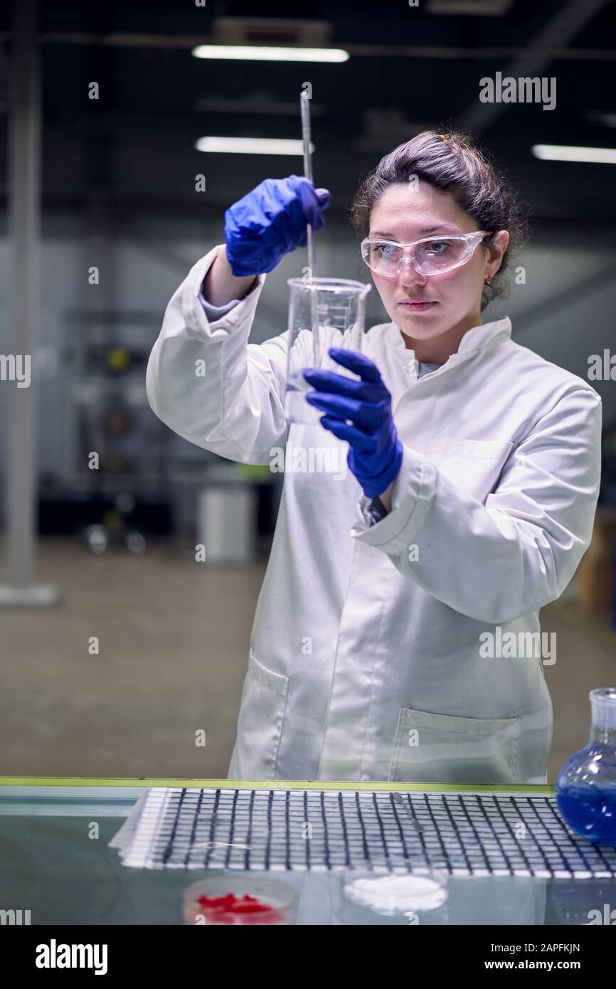 Serious lab woman in glasses and white coat with experimental glass in ...