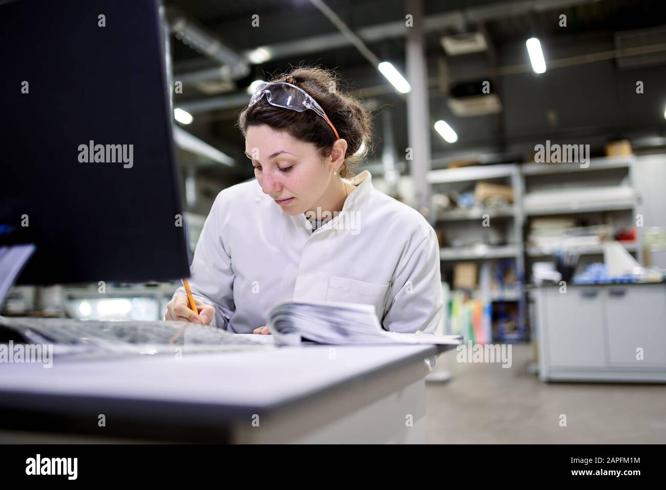 Serious brunette woman lab technician sitting at table with computer ...
