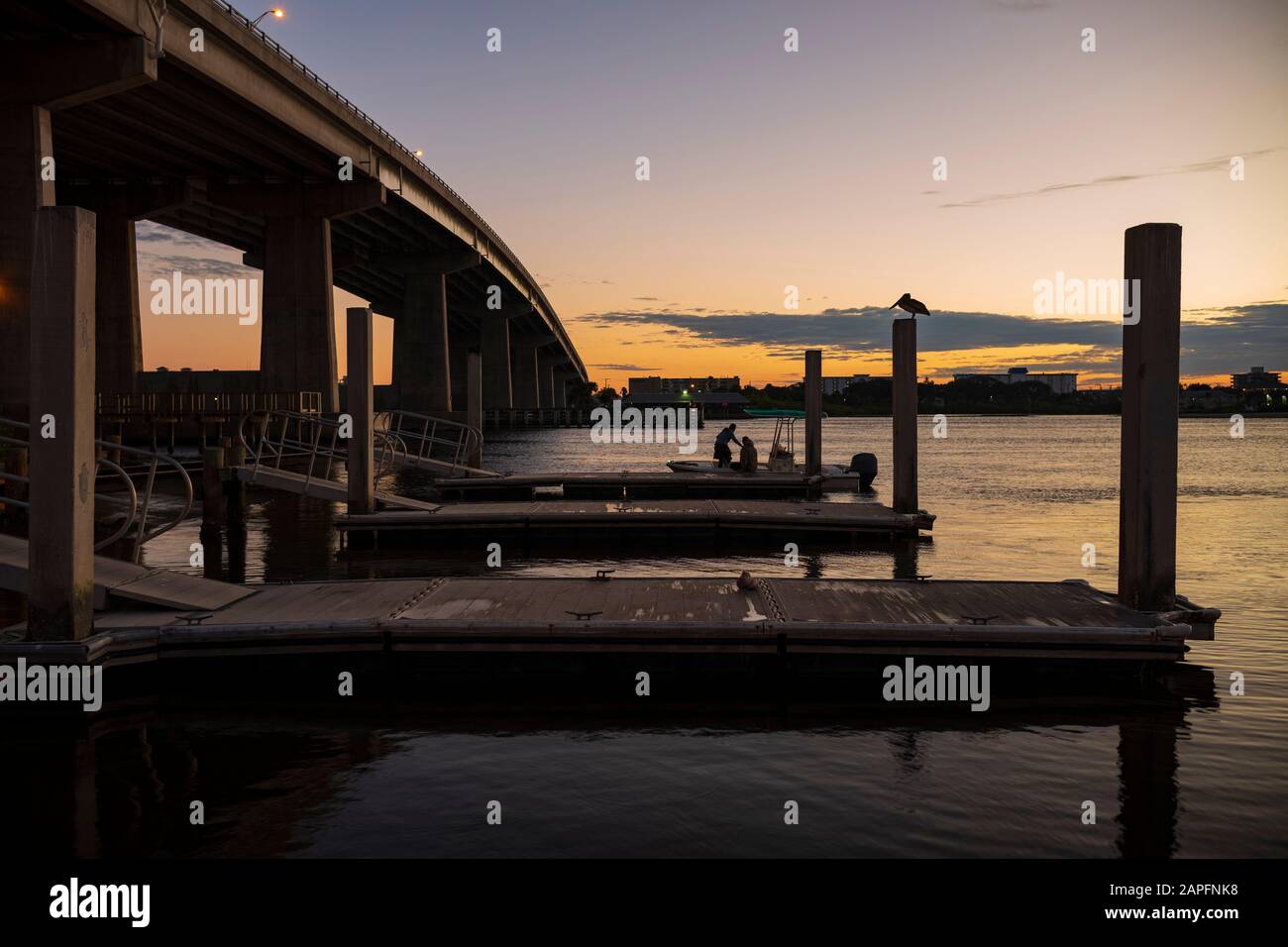 Silhouetted people boarding a boat for a fishing trip, off a pier in ...