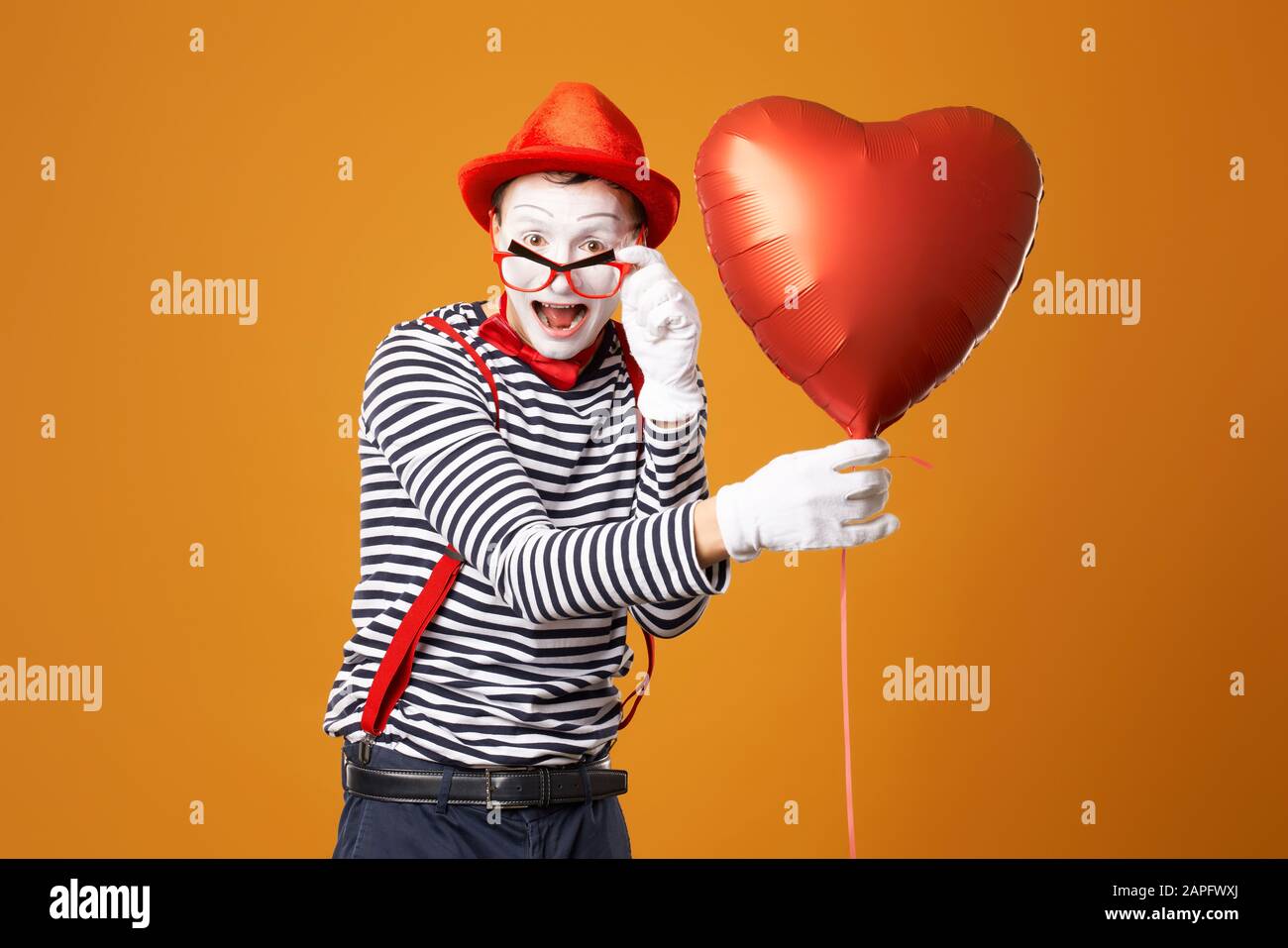Clown mime with heart ball on blank orange background Stock Photo - Alamy